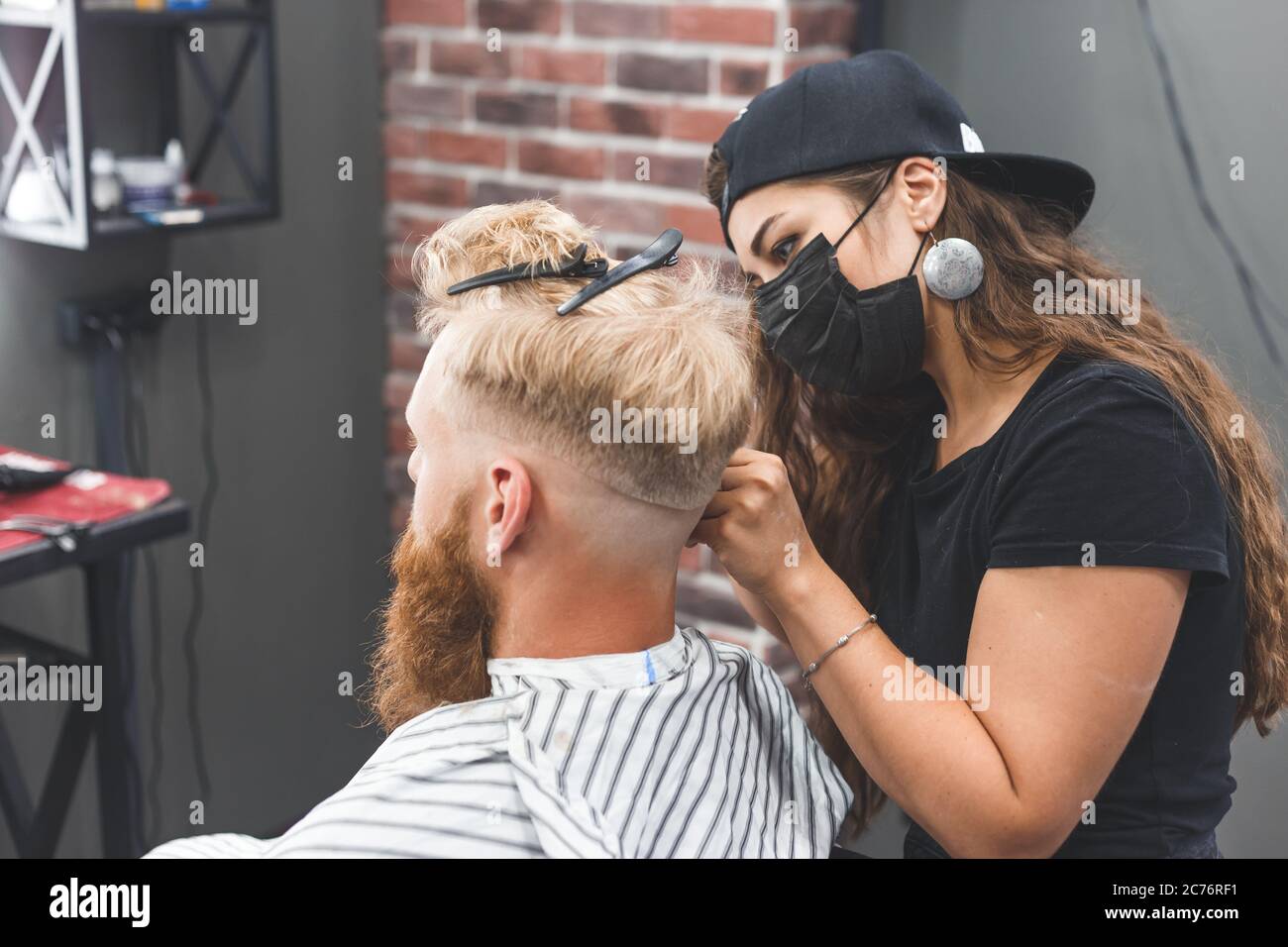 Female barber in mask cuts a man hairs with hair clipper. Hairstyle ...