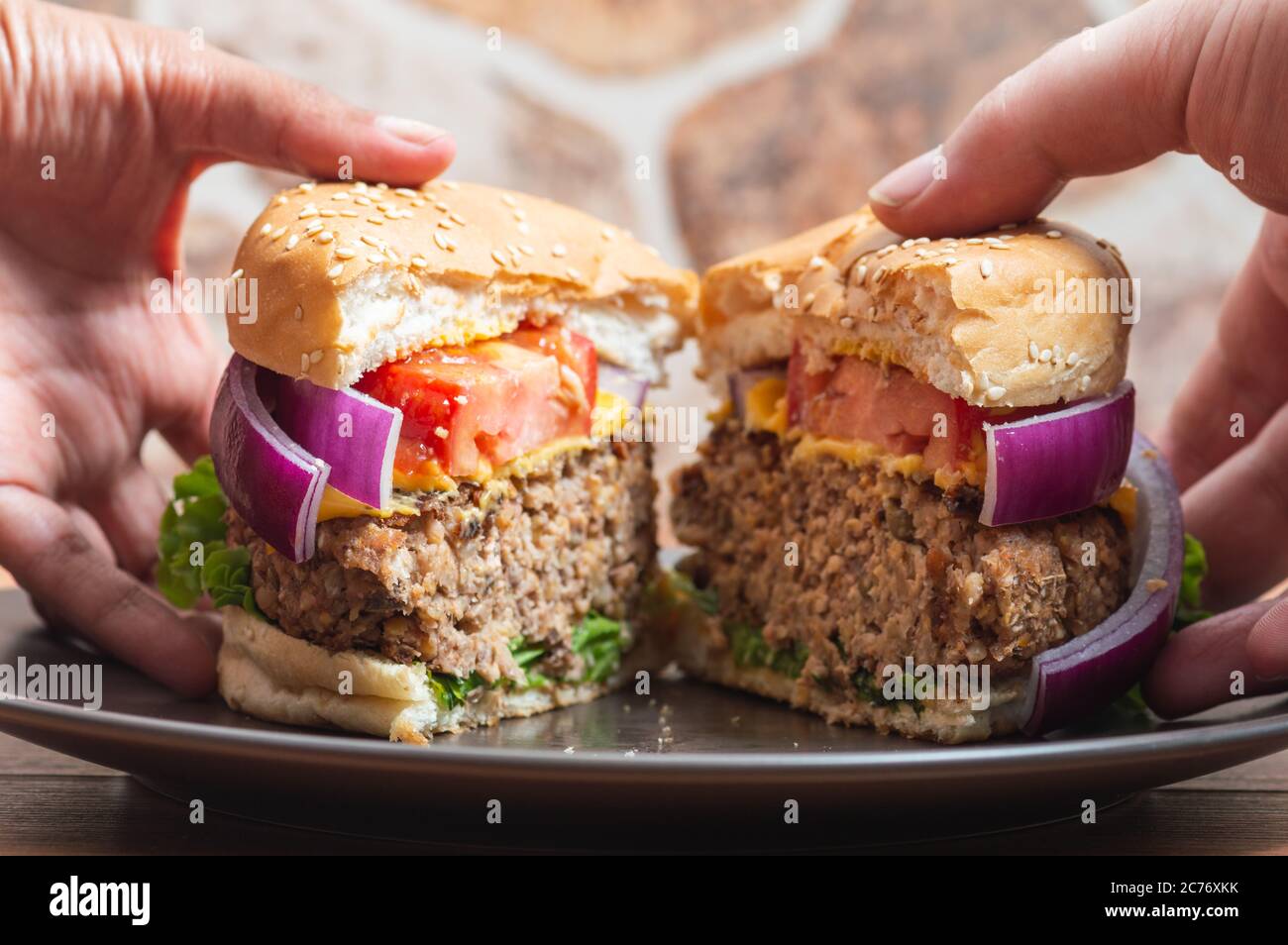 Two people's hands sharing a vegetarian burger made with beans and ...