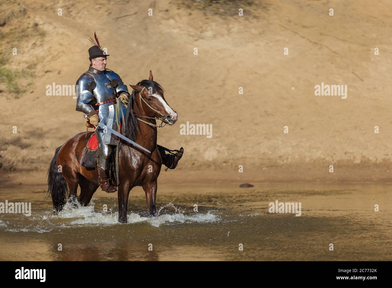 Adult man in ancient knight armor with a sword rides a horse on a river ...
