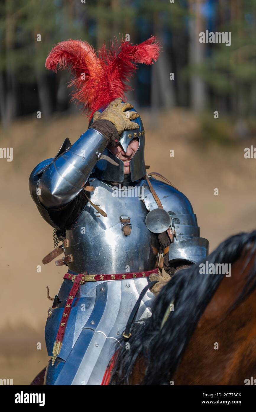 A young adult man in knightly armor rides a horse on a river along a ...