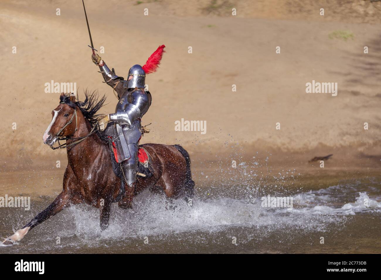 A young adult man in knightly armor rides a horse on a river along a ...