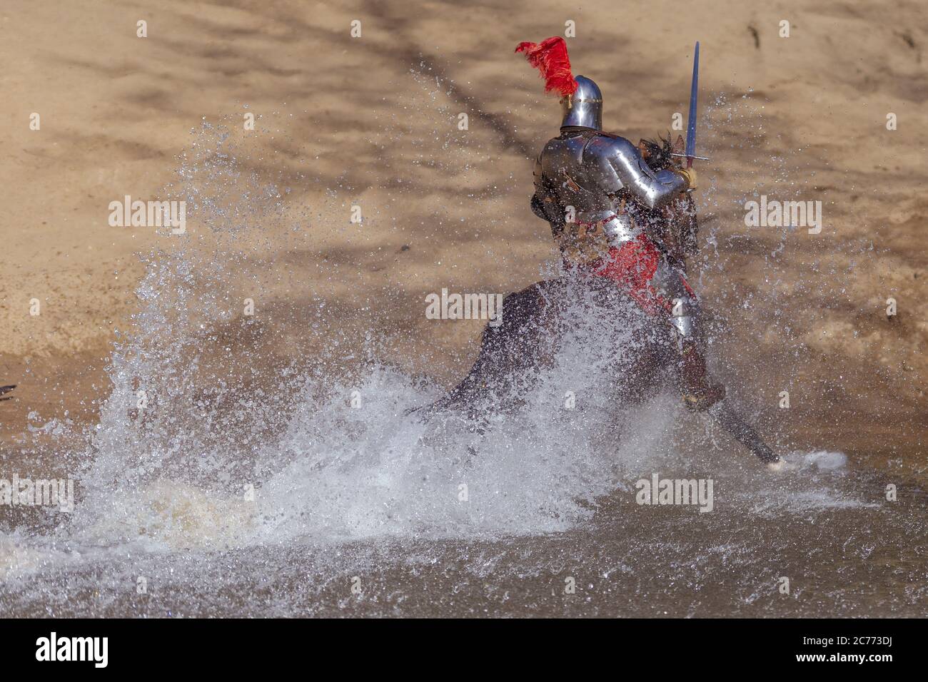 A young adult man in knightly armor rides a horse on a river along a ...