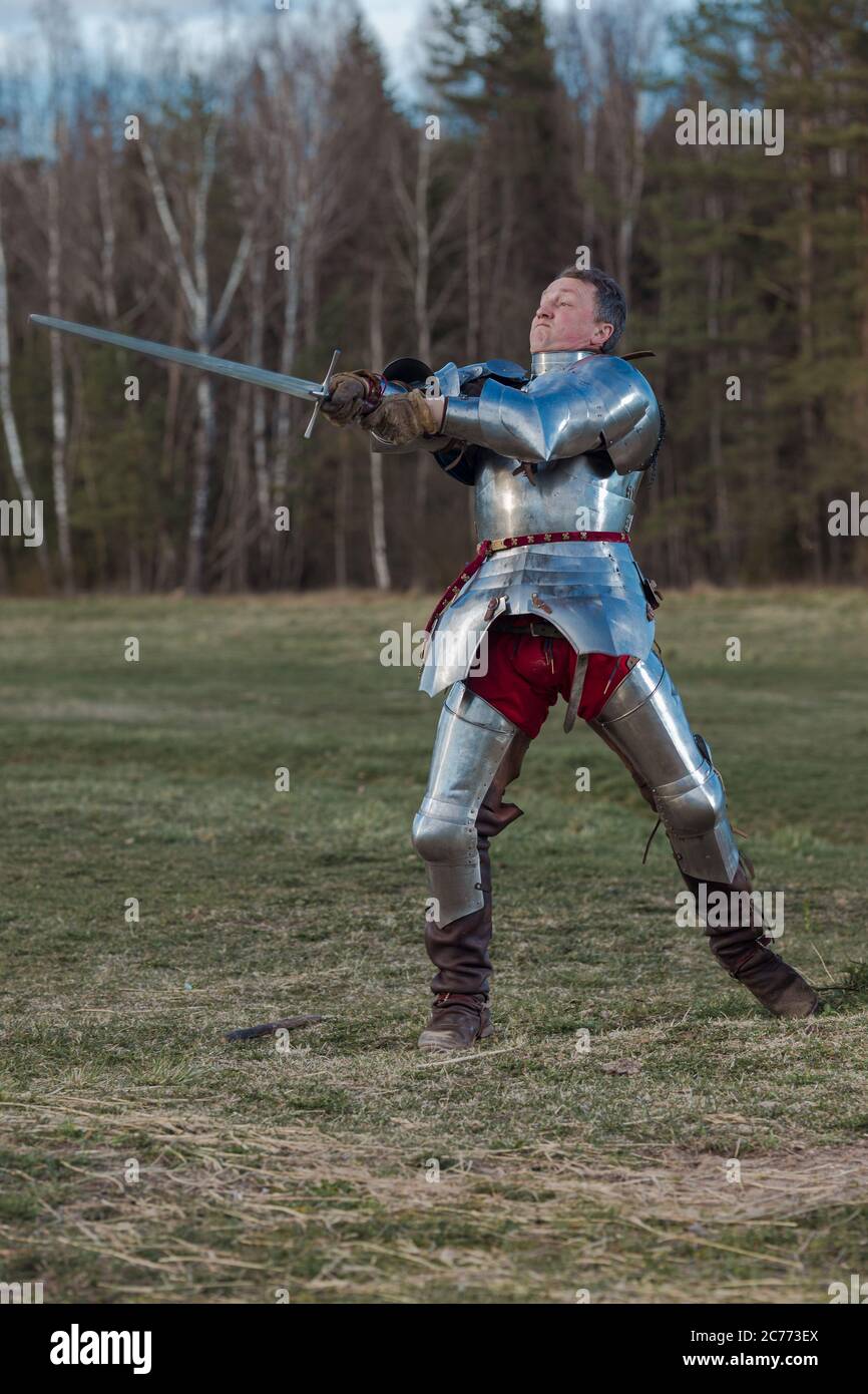 A walking knight in armor and holding a sword in his hands shows combat ...