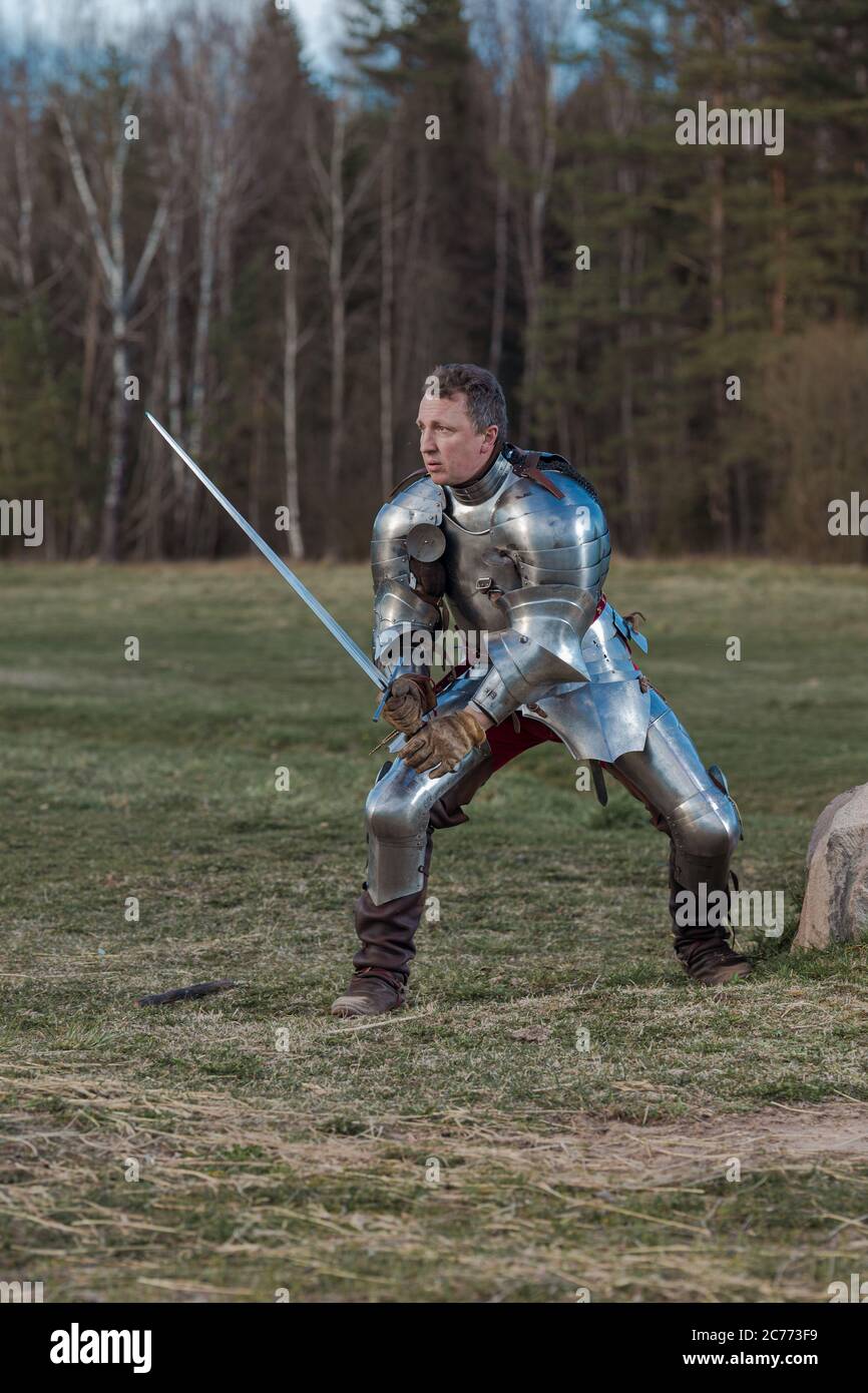 A walking knight in armor and holding a sword in his hands shows combat ...
