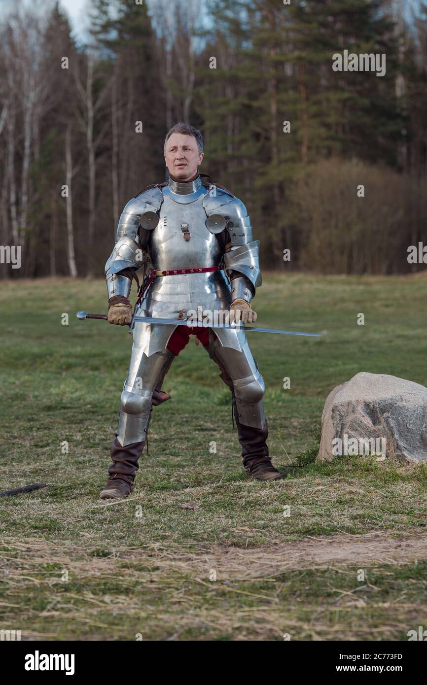 A walking knight in armor and holding a sword in his hands shows combat ...