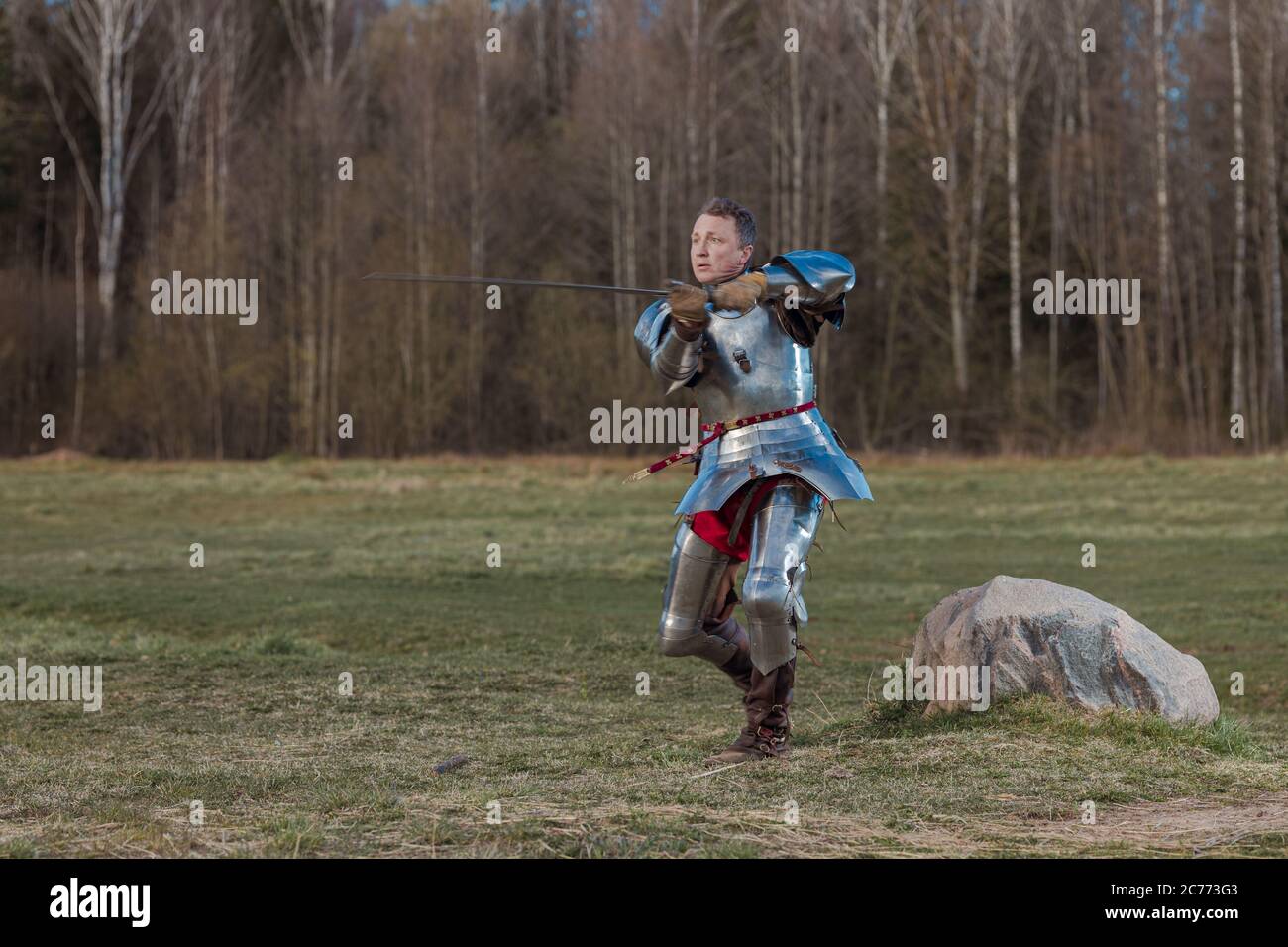 A walking knight in armor and holding a sword in his hands shows combat ...