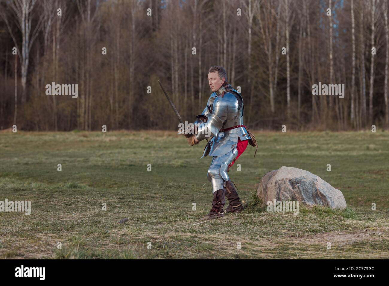A walking knight in armor and holding a sword in his hands shows combat ...