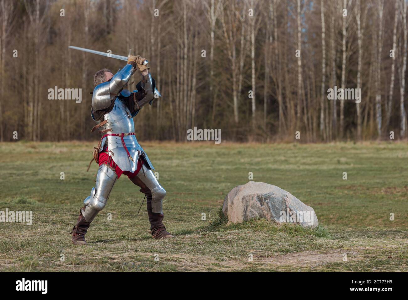 A walking knight in armor and holding a sword in his hands shows combat ...