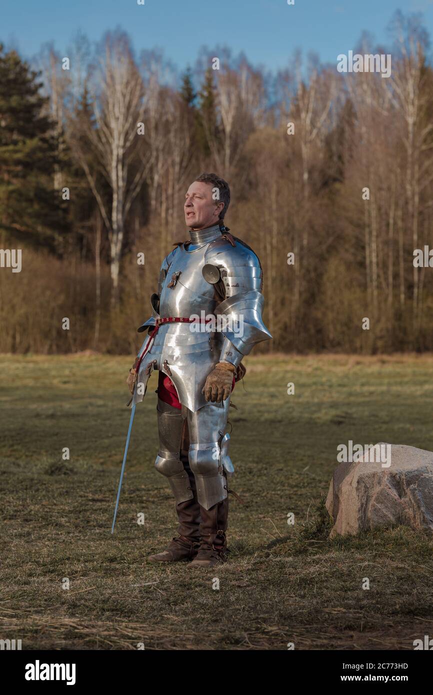 A walking knight in armor and holding a sword in his hands shows combat ...