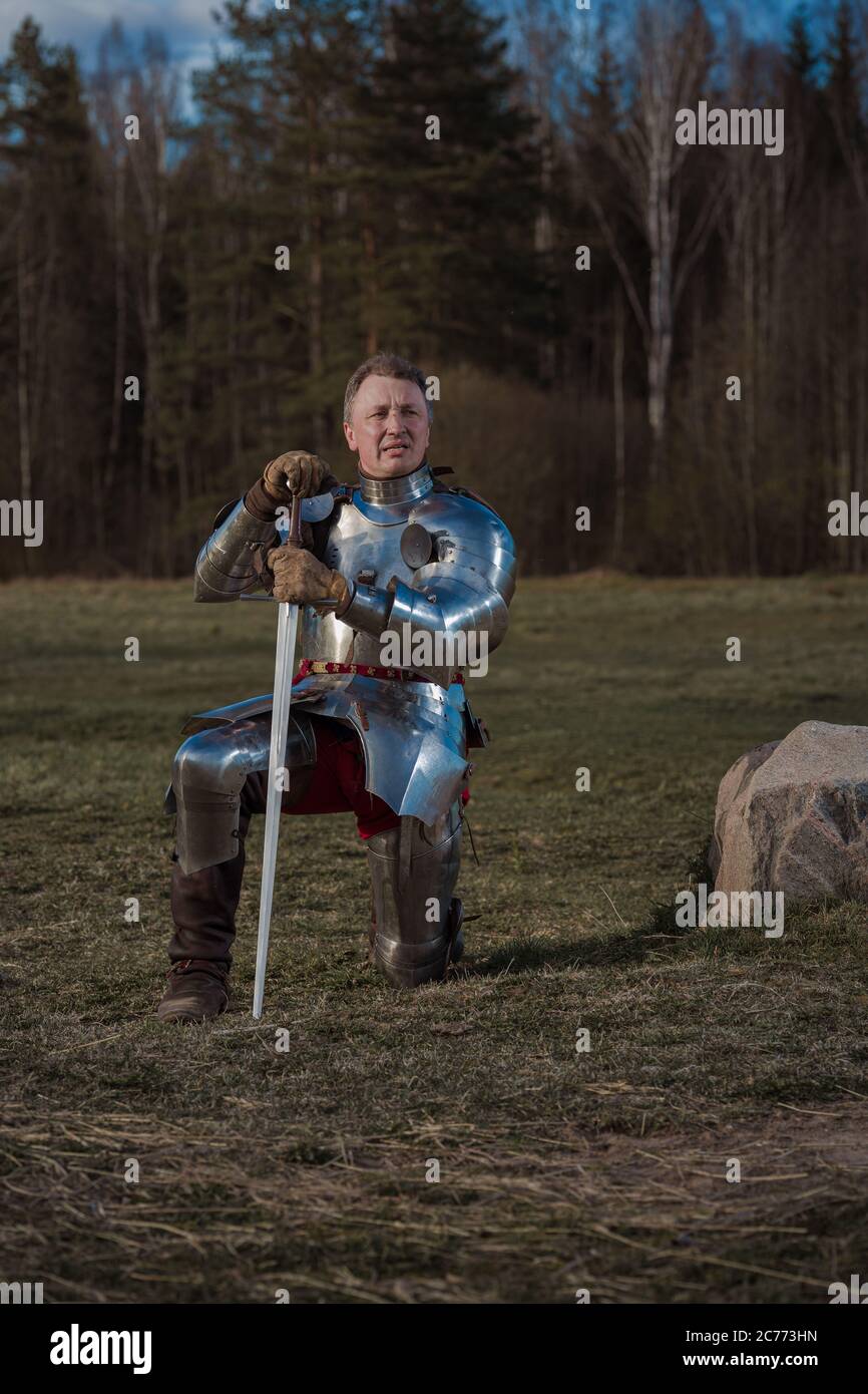 A walking knight in armor and holding a sword in his hands shows combat ...