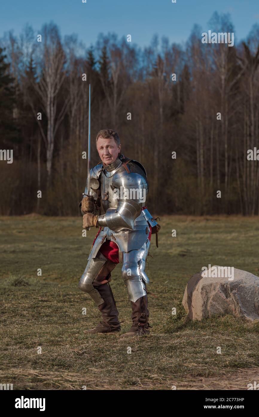 A walking knight in armor and holding a sword in his hands shows combat ...