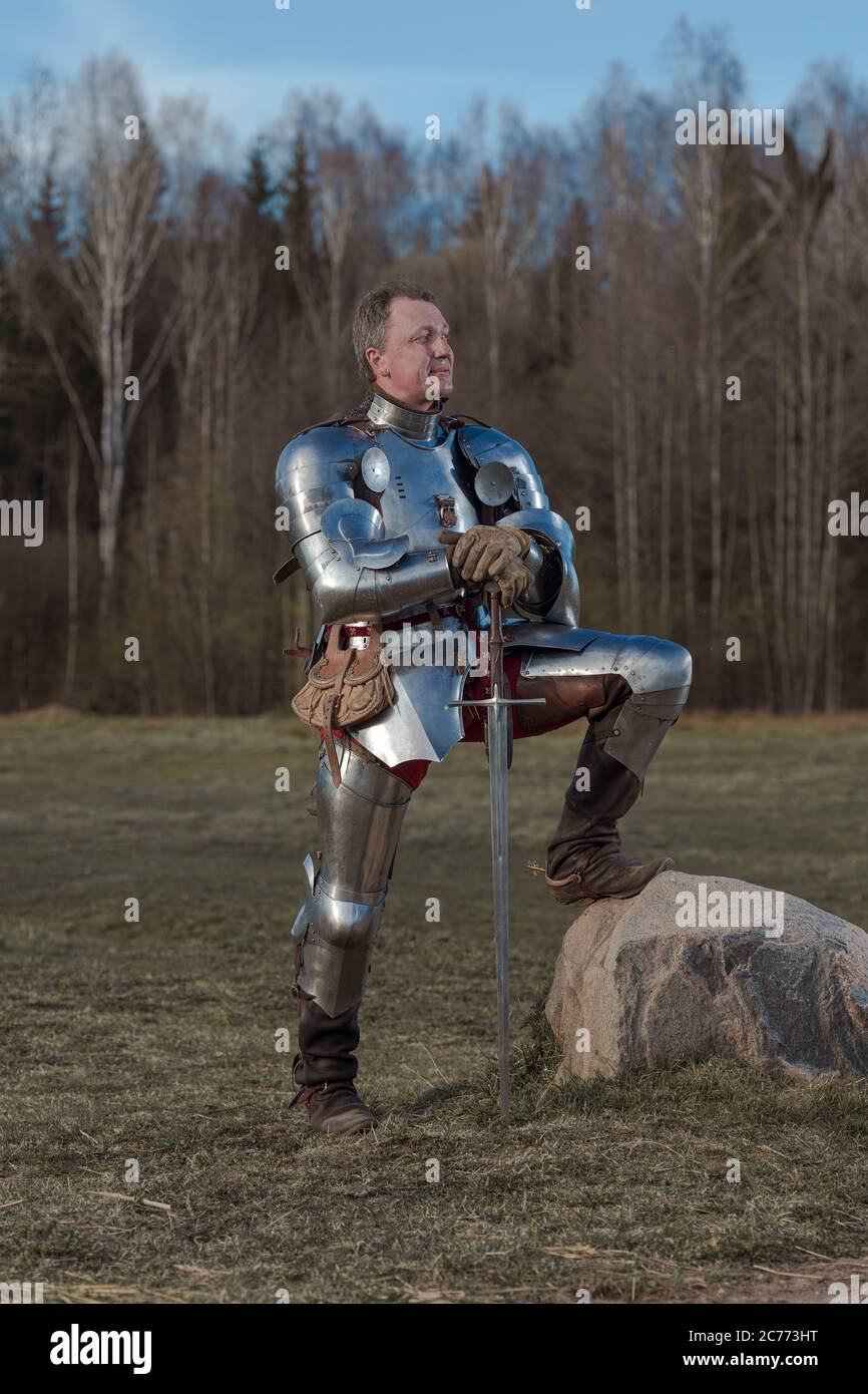 A walking knight in armor and holding a sword in his hands shows combat ...