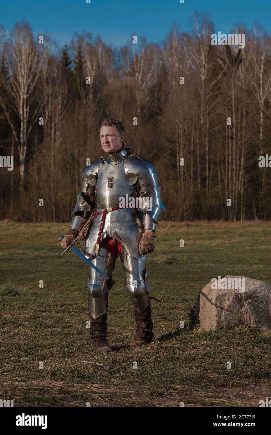 A walking knight in armor and holding a sword in his hands shows combat ...