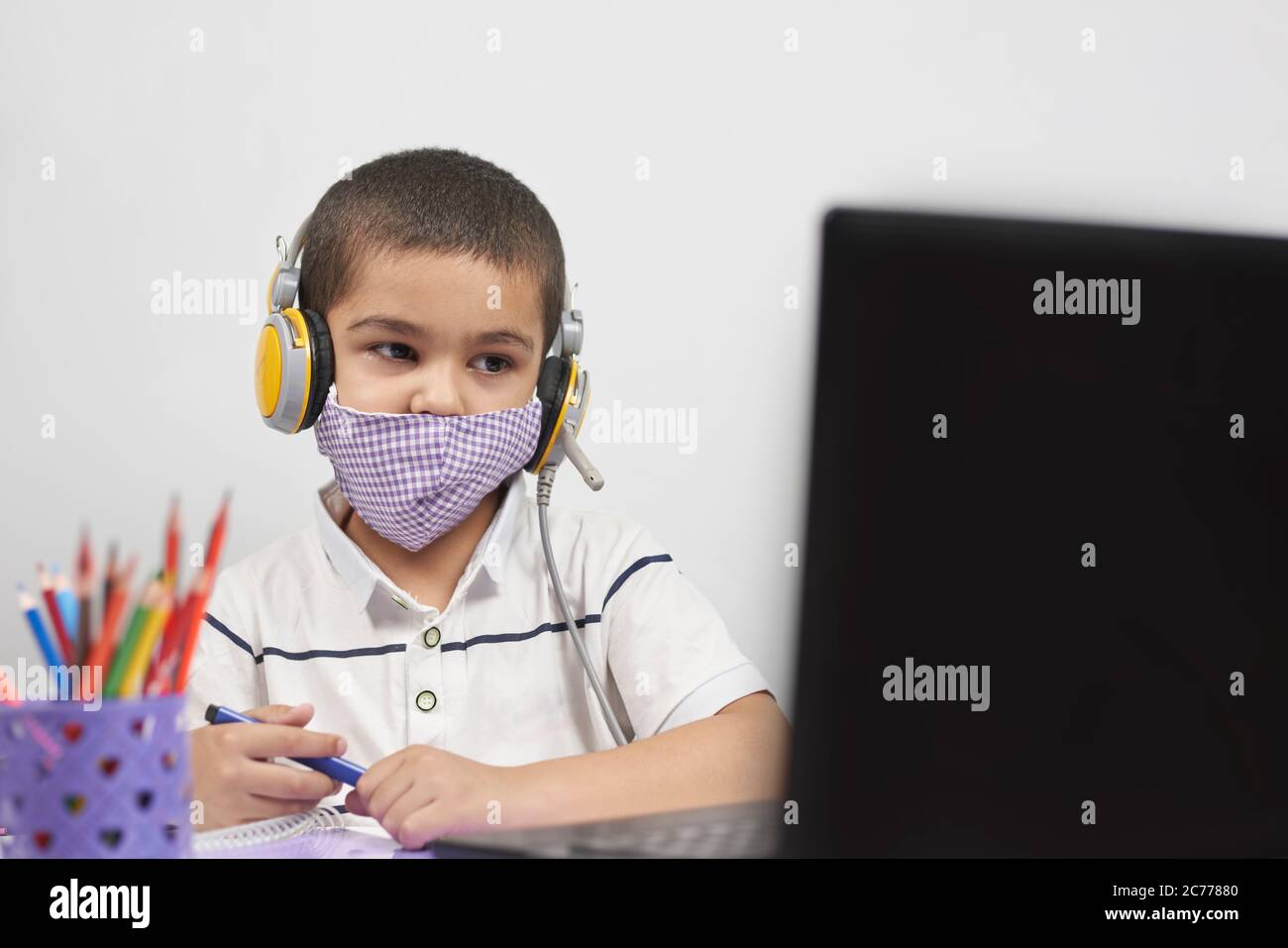 Young kid in headphones doing online exercises via laptop. Learning ...
