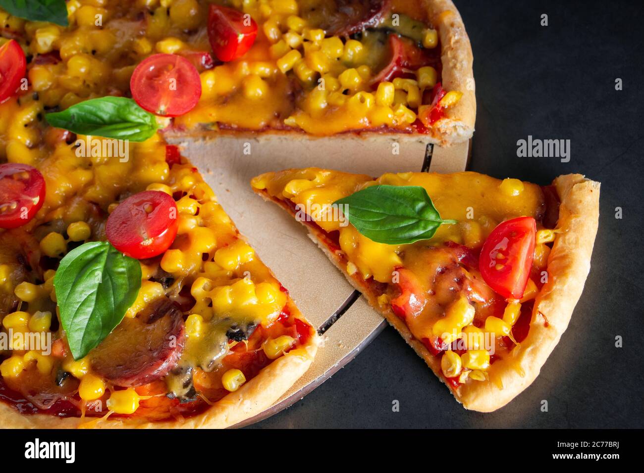 Tasty pizza with cherry tomatoes and sliced slice on a black background ...