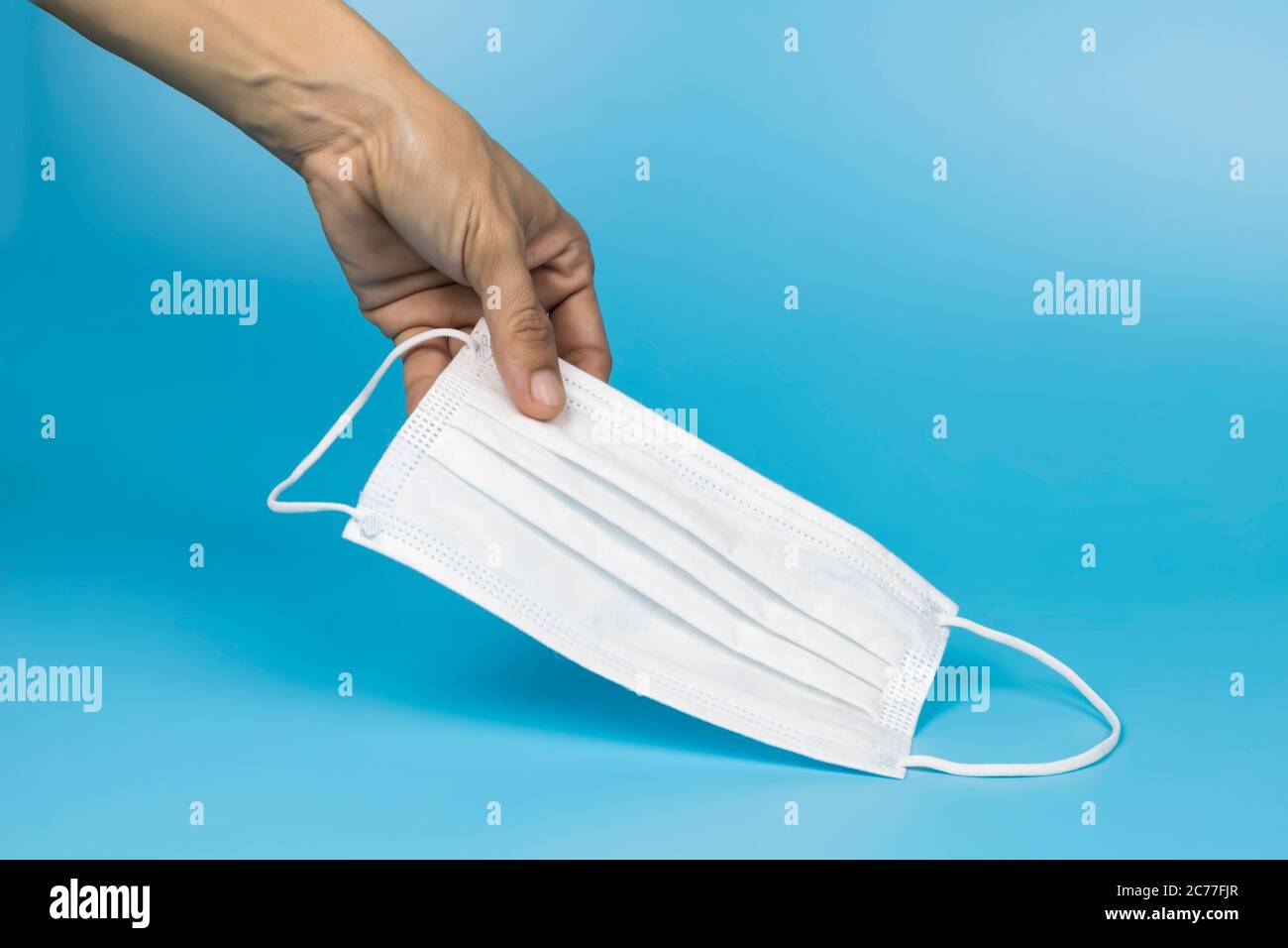 Women hand pickup and hold medical face mask on blue background. Women ...