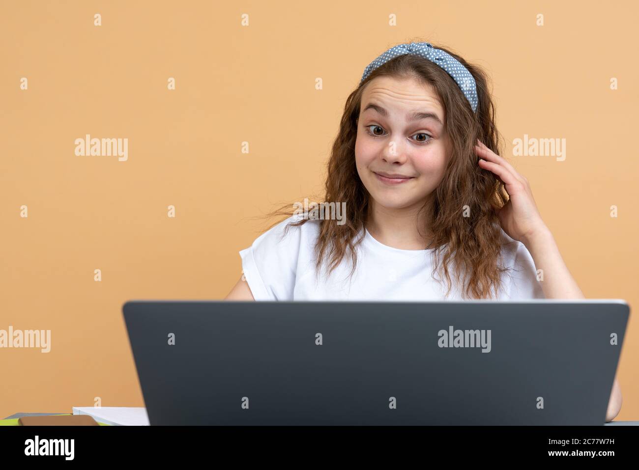 Pensive young girl sit by the table at home with laptop thinking over ...