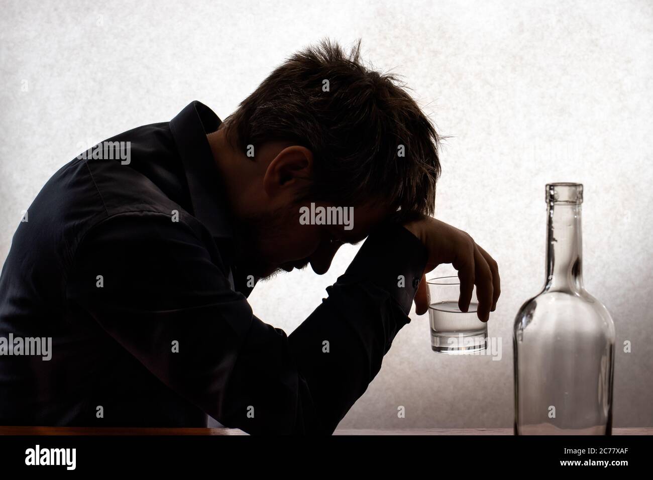 A silhouetted photo. A man in alcoholic intoxication holds a glass of ...
