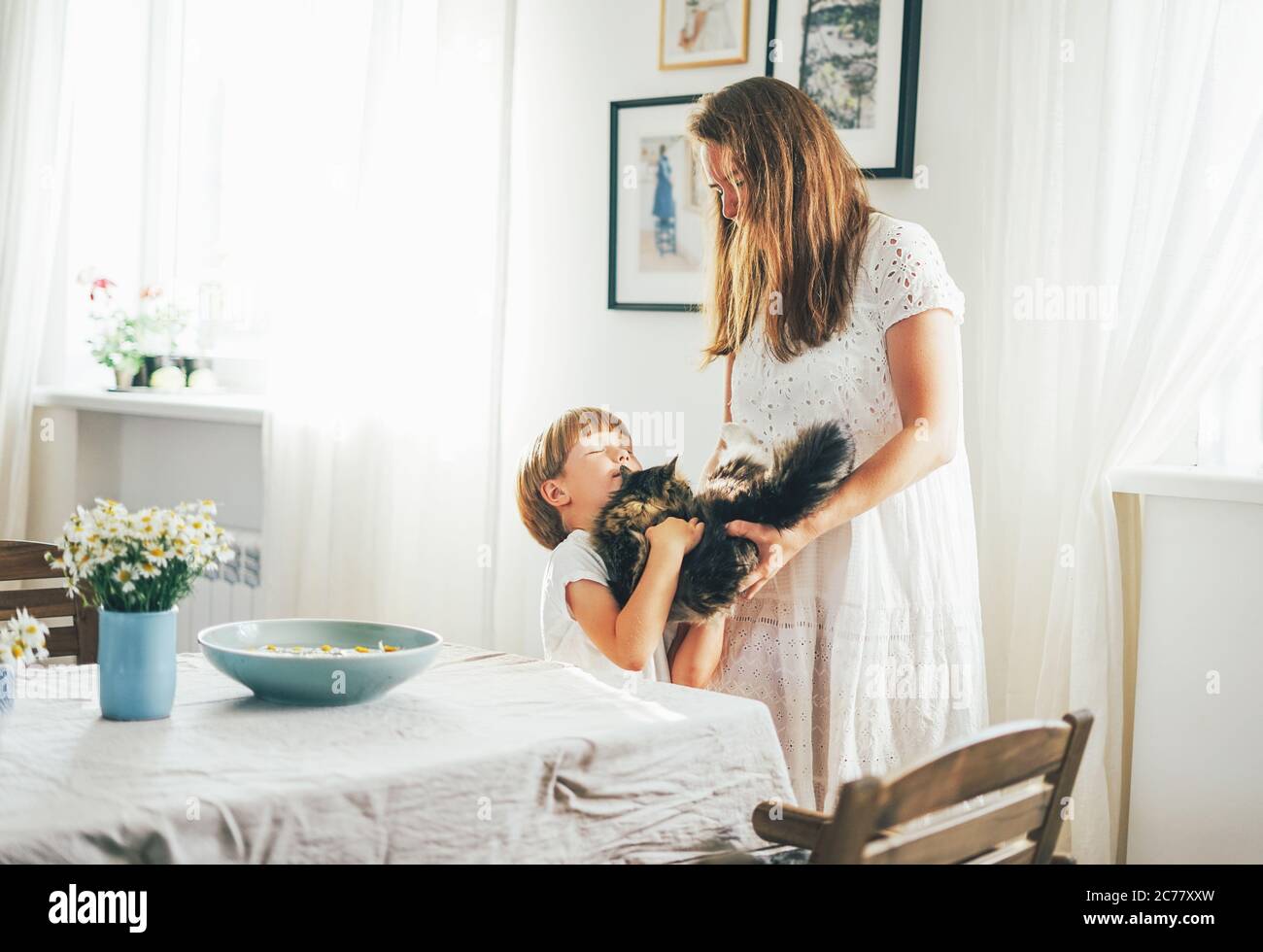 Cute blonde toddler boy with cat on hands and his mother at bright ...
