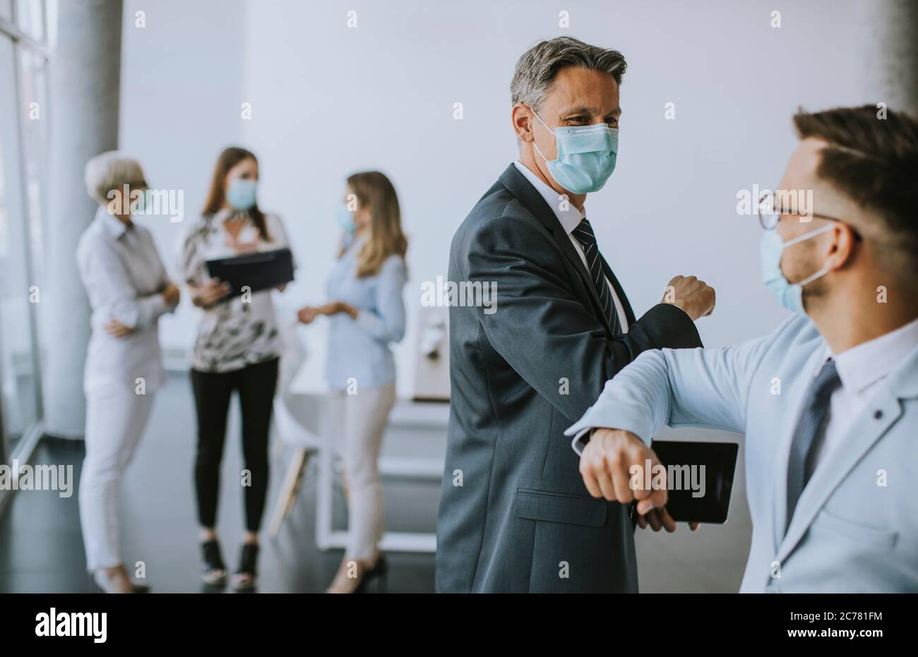 Two colleagues avoid a handshake when meeting in the office and greet ...