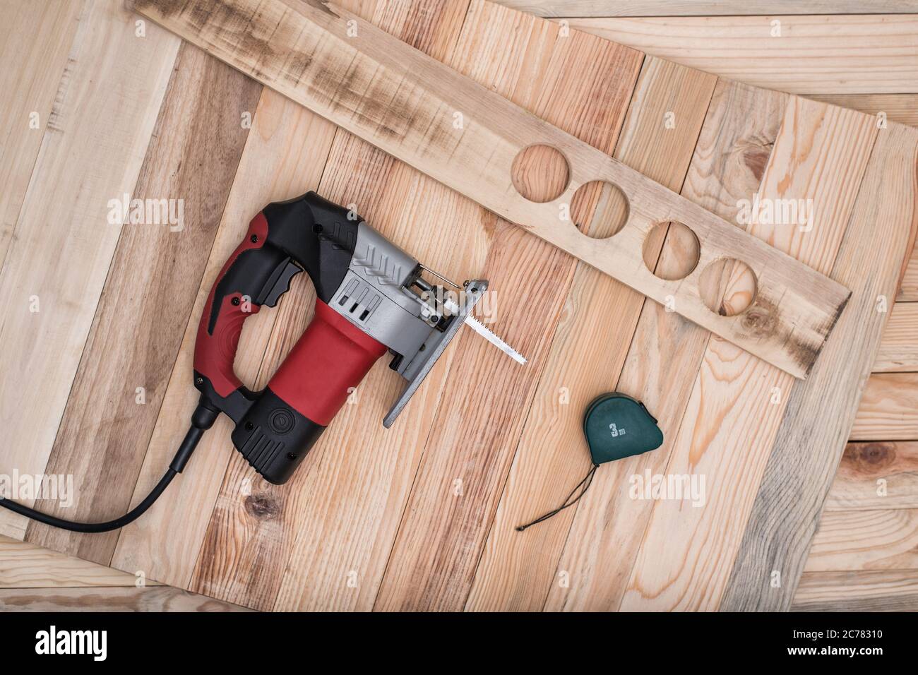Electric jigsaw, measuring tape and workpiece lying on a light brown ...