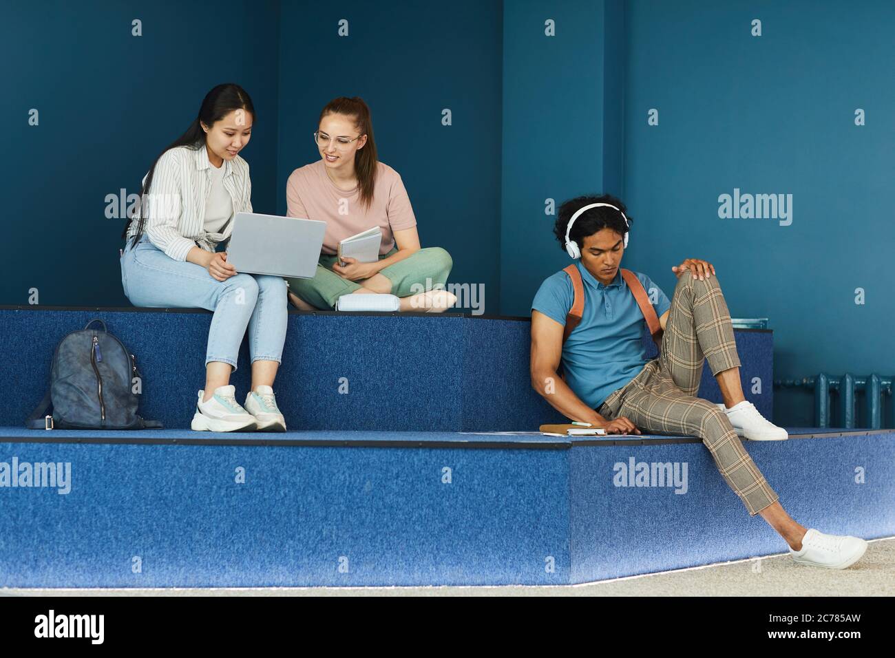 Multi-ethnic university students sitting on steps and using workbooks ...