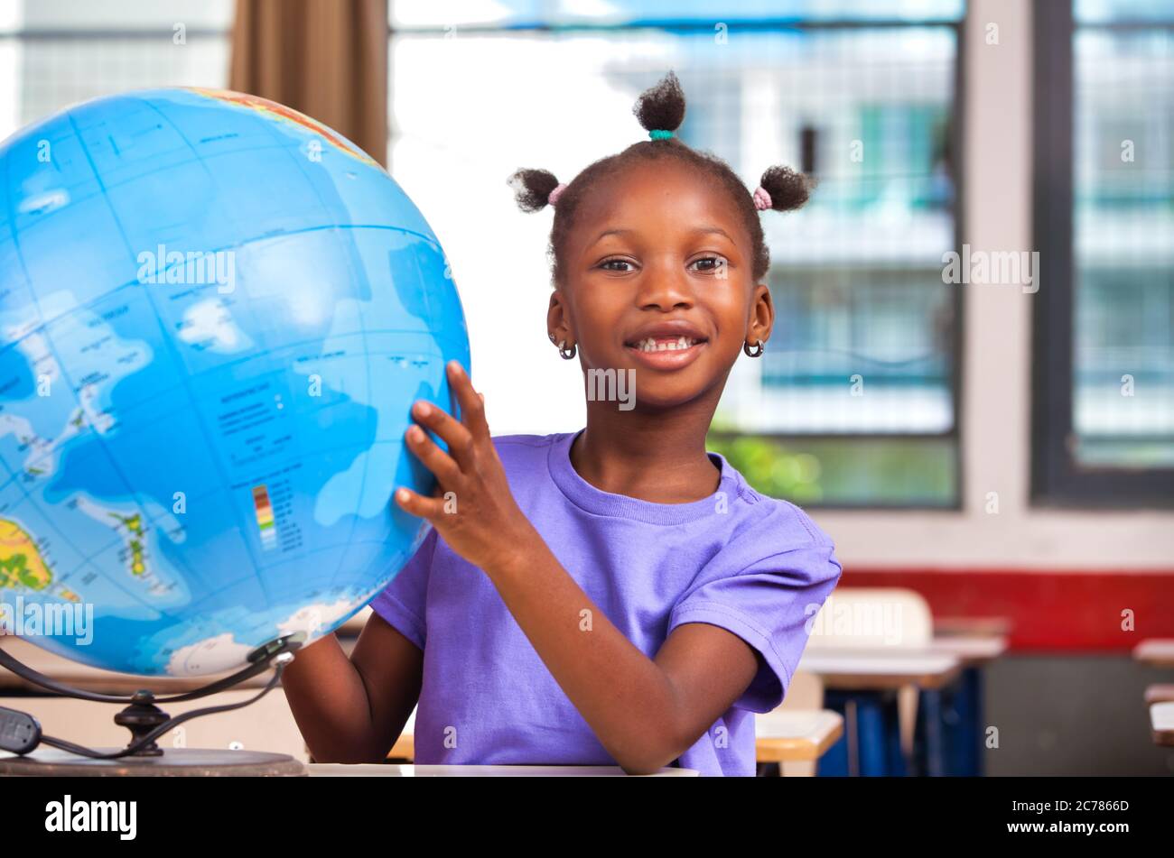 Elementary school scene. African schoolgirl using world globe in the ...