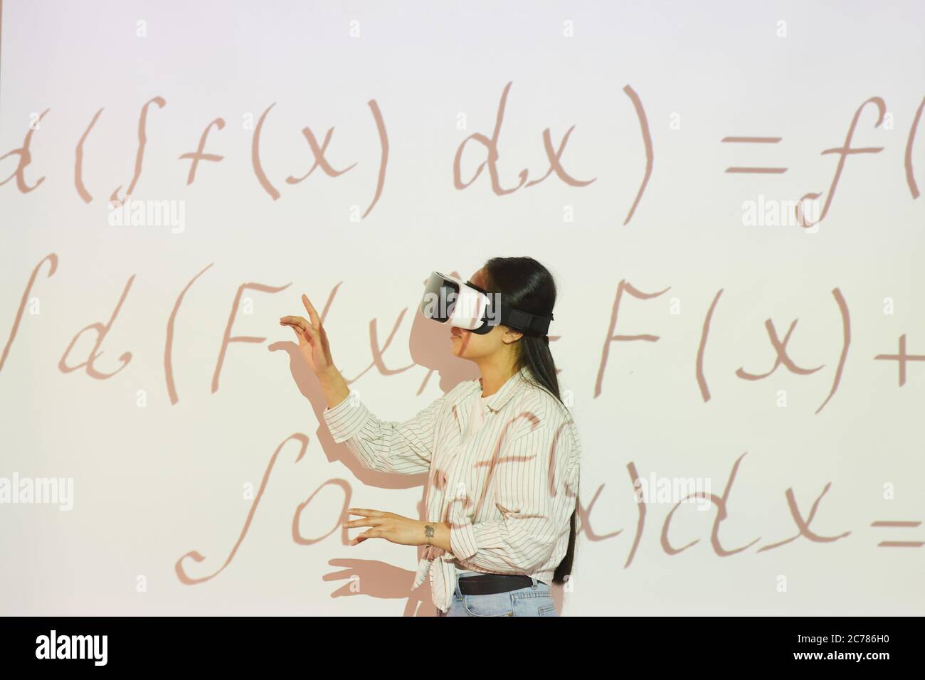 Brunette student girl in virtual reality headset pointing at projection ...