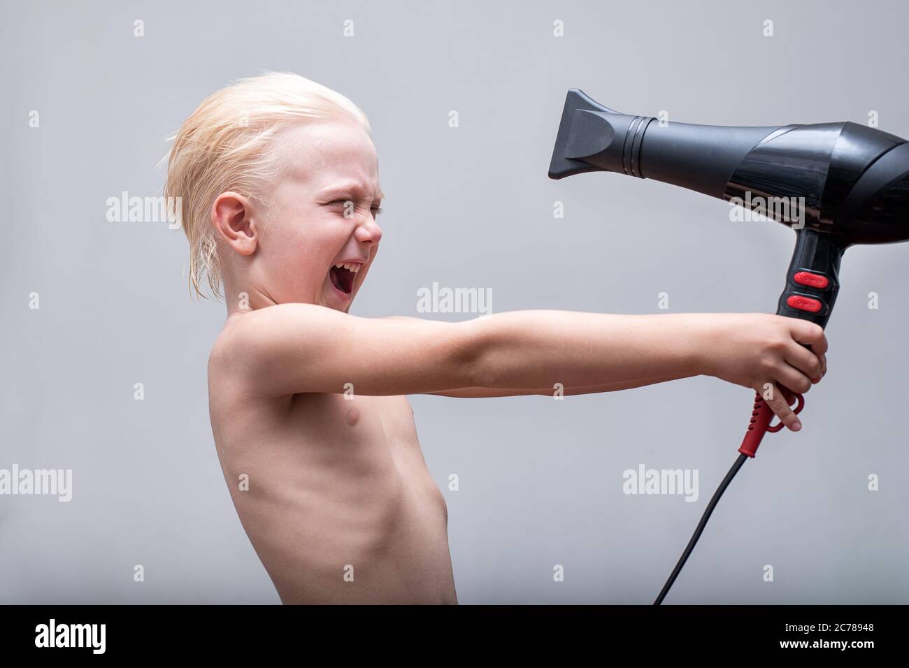 Blond boy with wet hair is funny dried by a hairdryer. White background ...