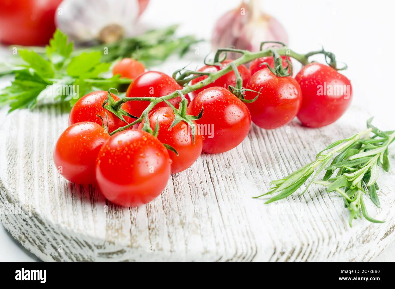 Bunch of juicy organic red cherry tomatoes with green rosemary, garlic and spices on white old ...