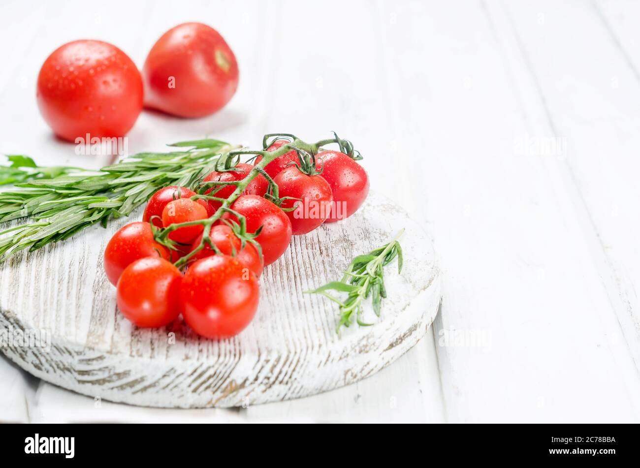 Bunch of juicy organic red cherry tomatoes with green rosemary, garlic and spices on white old ...