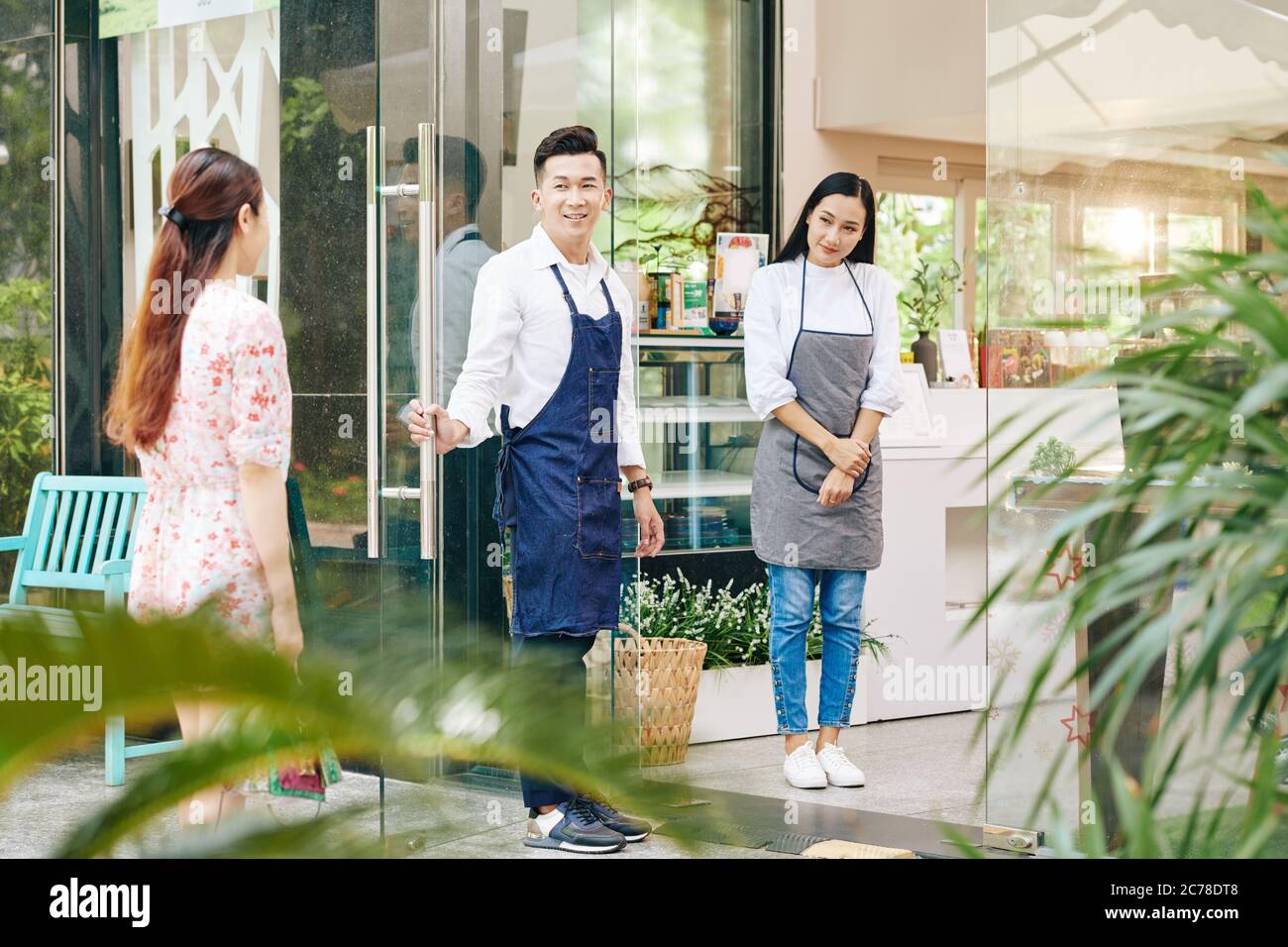 Smiling young waiters standing at cafe entrance doors and inviting ...