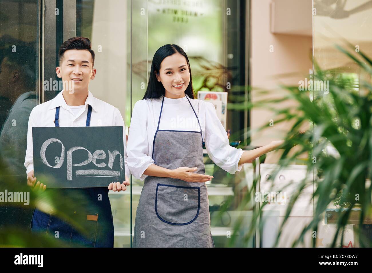 Smiling young waiter showing opend sign when waitress making welcoming ...