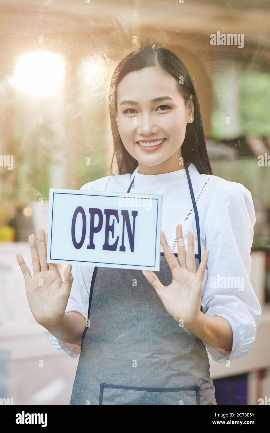 Portrait of pretty young Vietnamese waitress sticking sign on cafe door ...