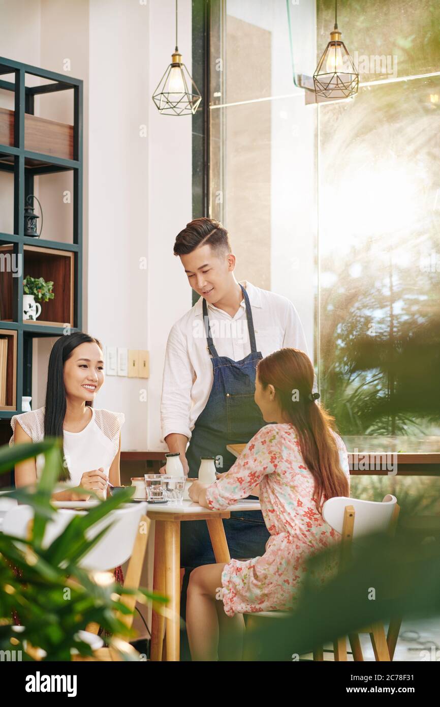 Smiling young Vietnamese waiter serving delicious breakfast to young ...