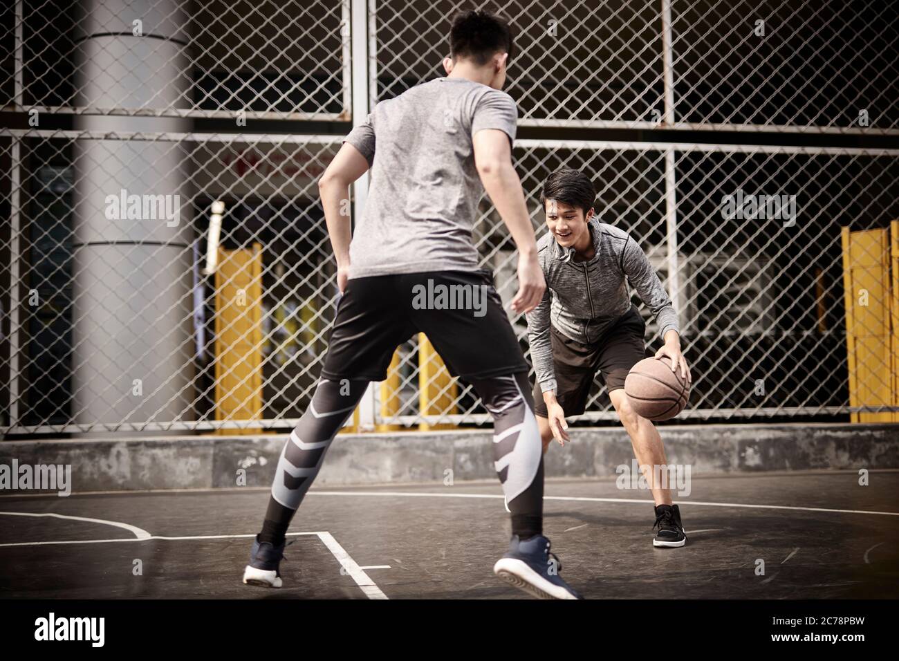 two young asian adult men playing one-on-one basketball on outdoor ...