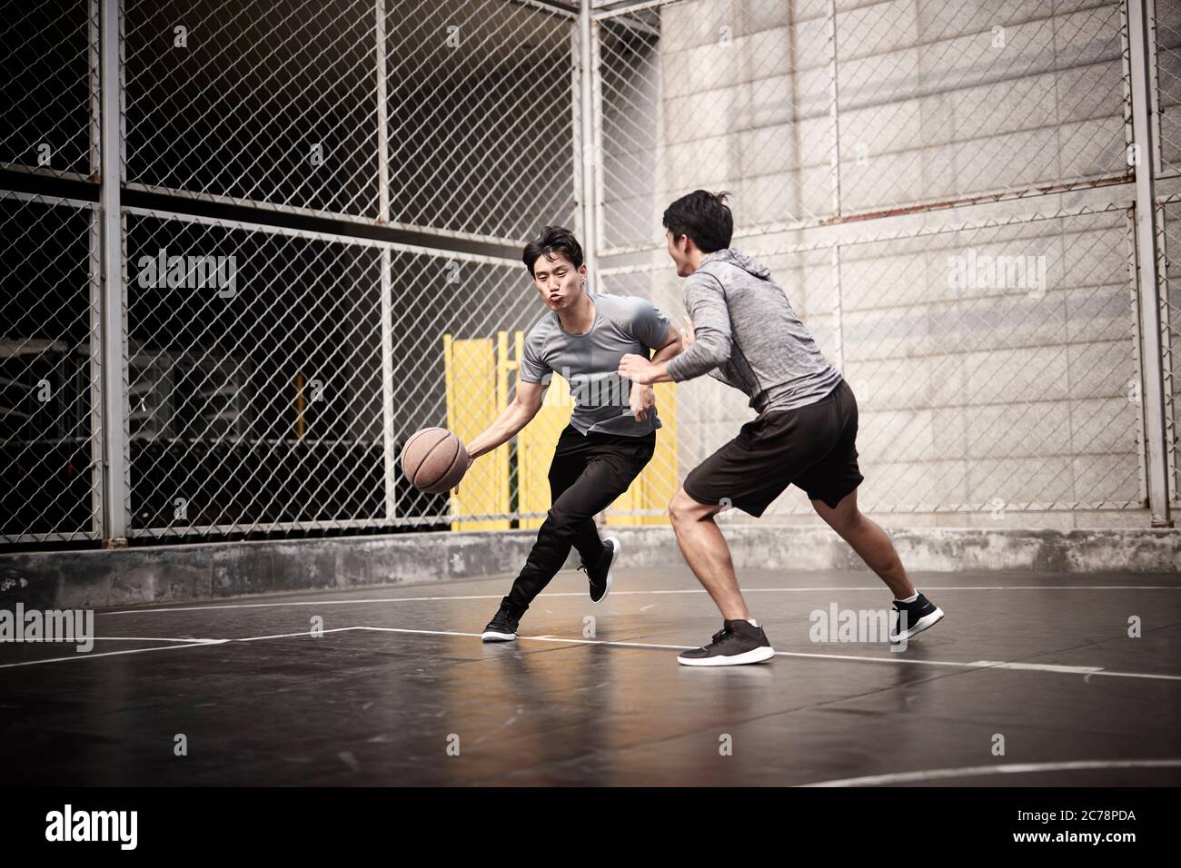 two young asian adult men playing one-on-one basketball on outdoor ...
