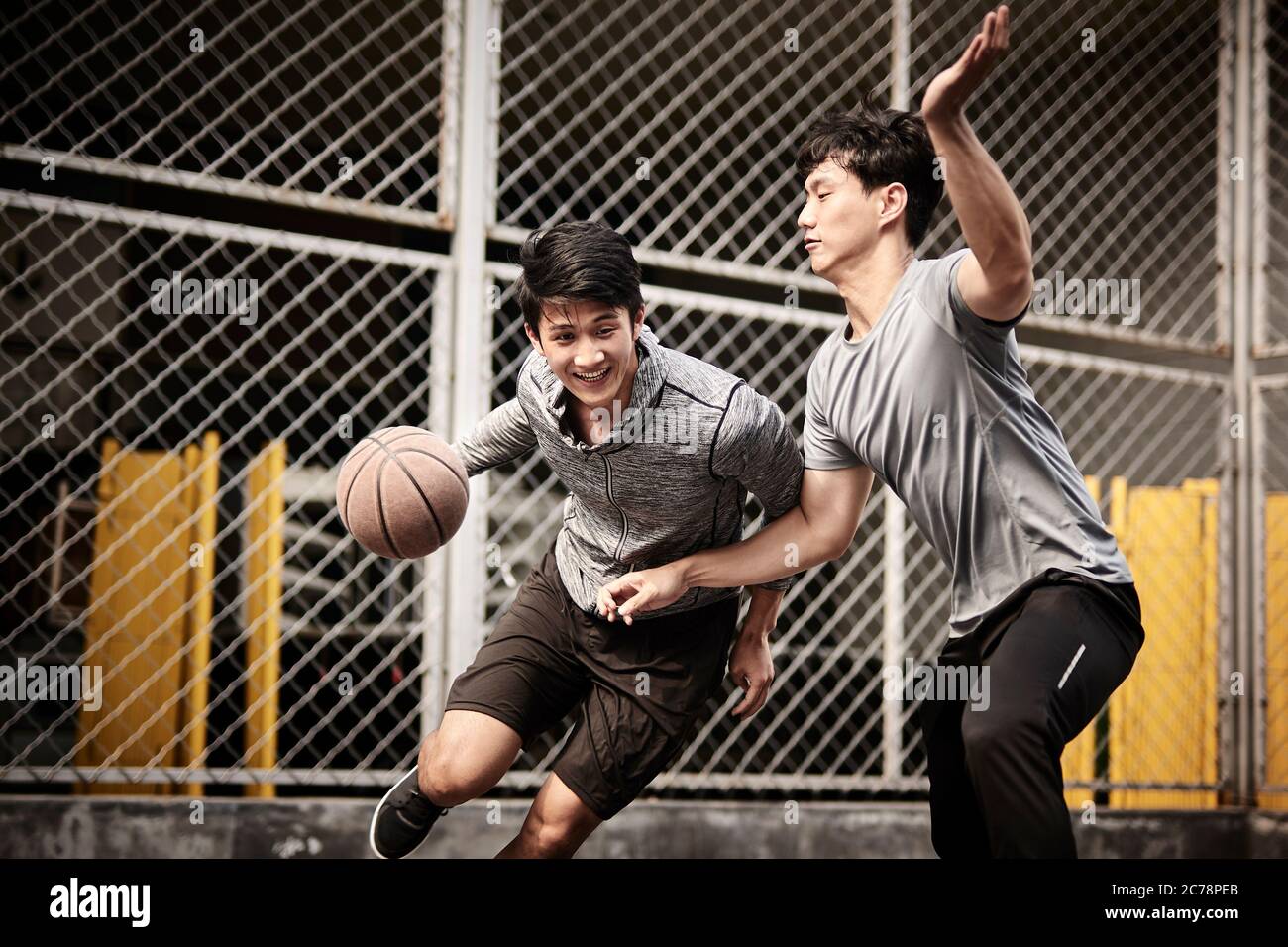two young asian adult men playing one-on-one basketball on outdoor ...