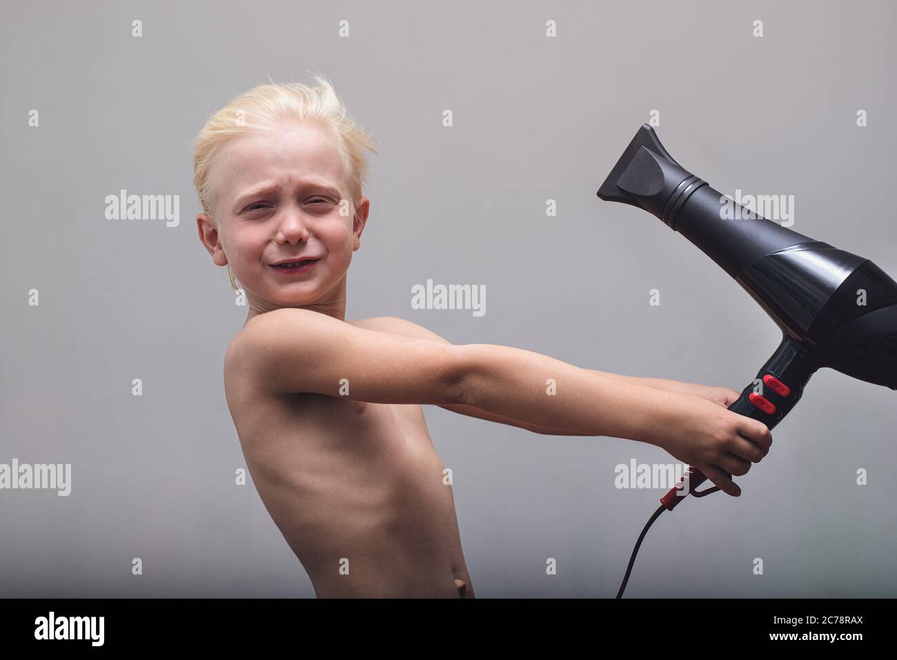 Blond boy with wet hair is funny dried by a hairdryer. White background ...