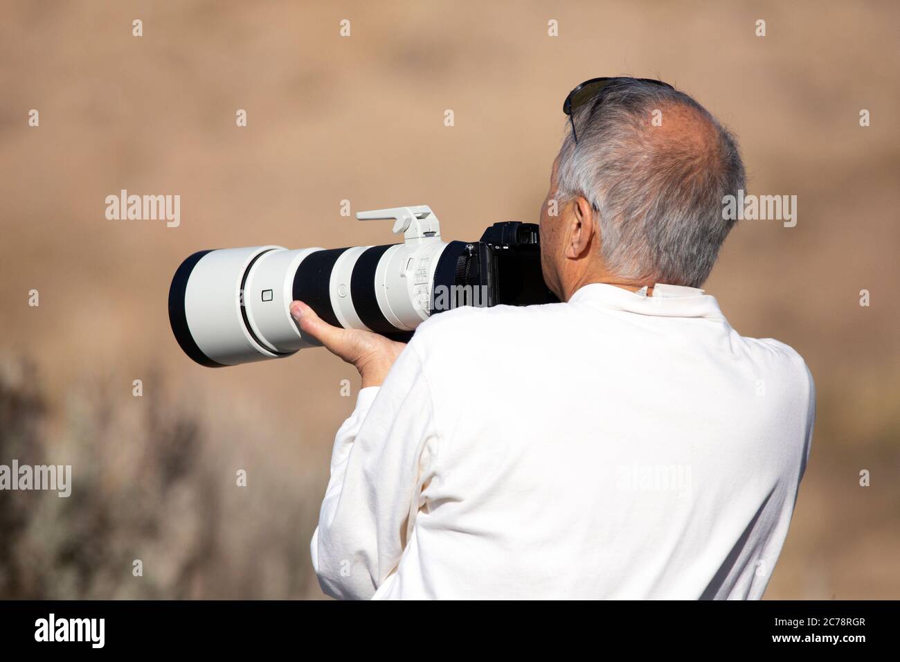Older man holding a large camera with a white telephoto lens in the ...