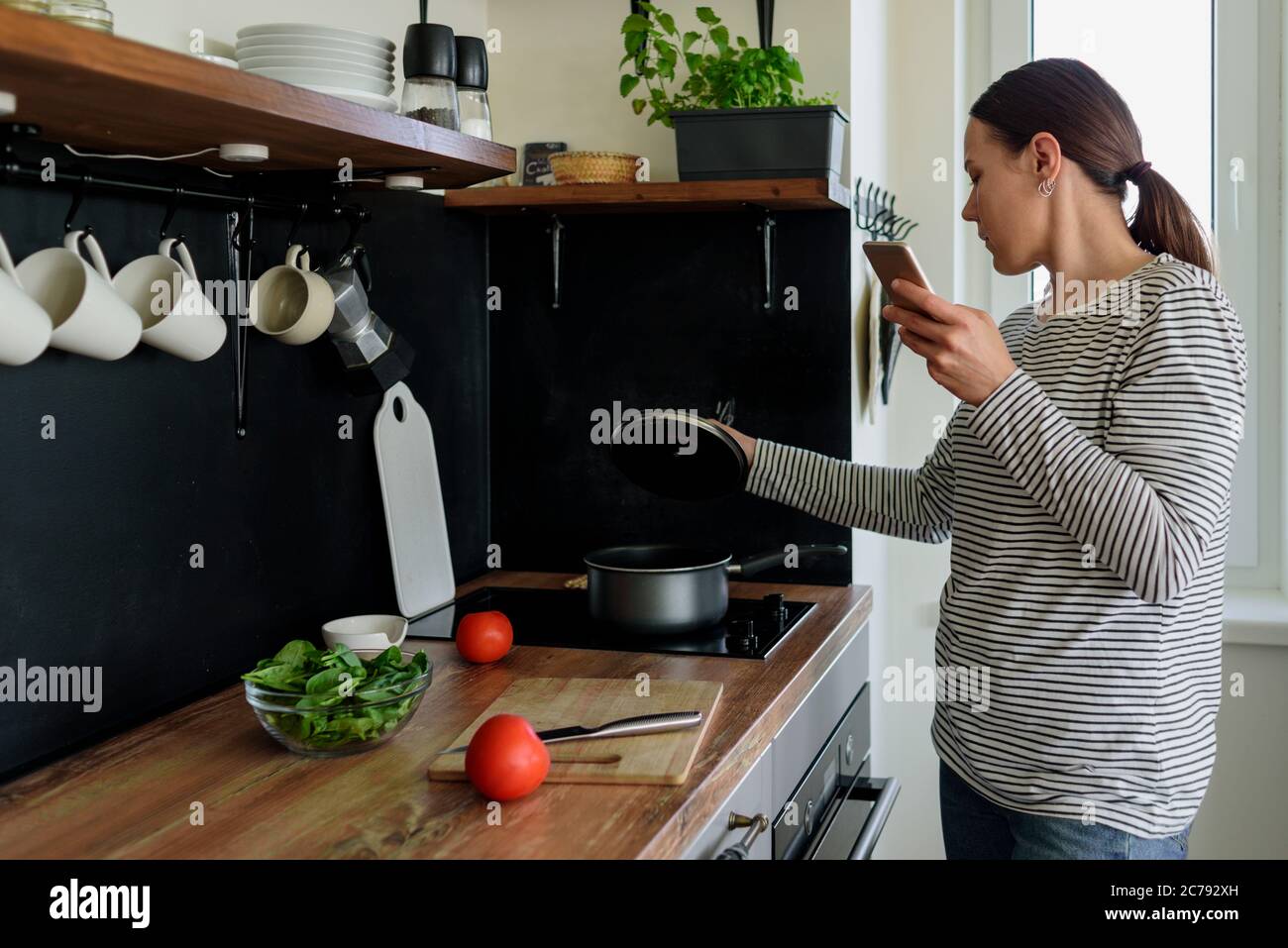 Woman using phone while cooking healthy food in kitchen Stock Photo - Alamy