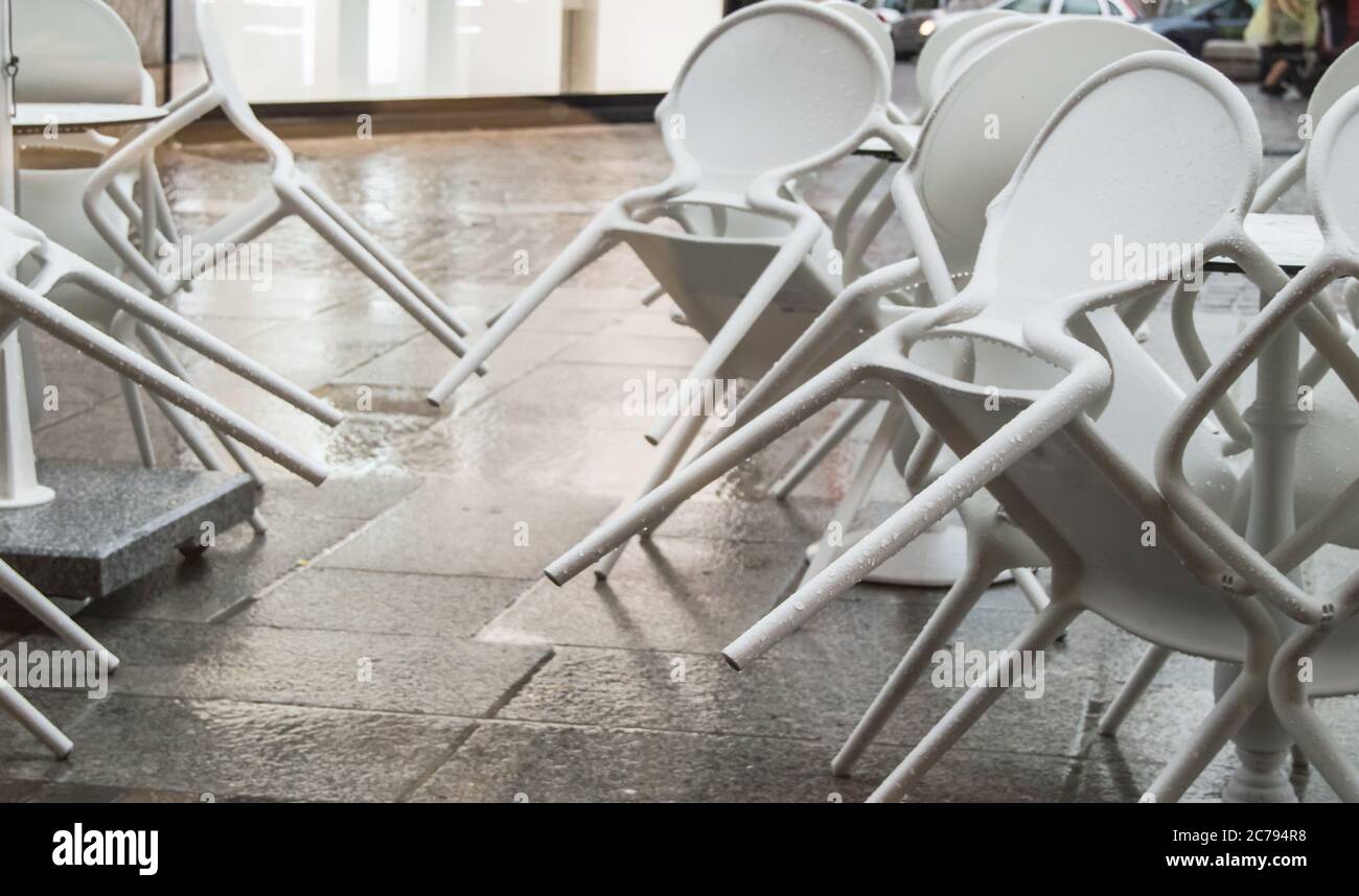 Wet white plastic chairs with raindrops in a street cafe, overturned ...