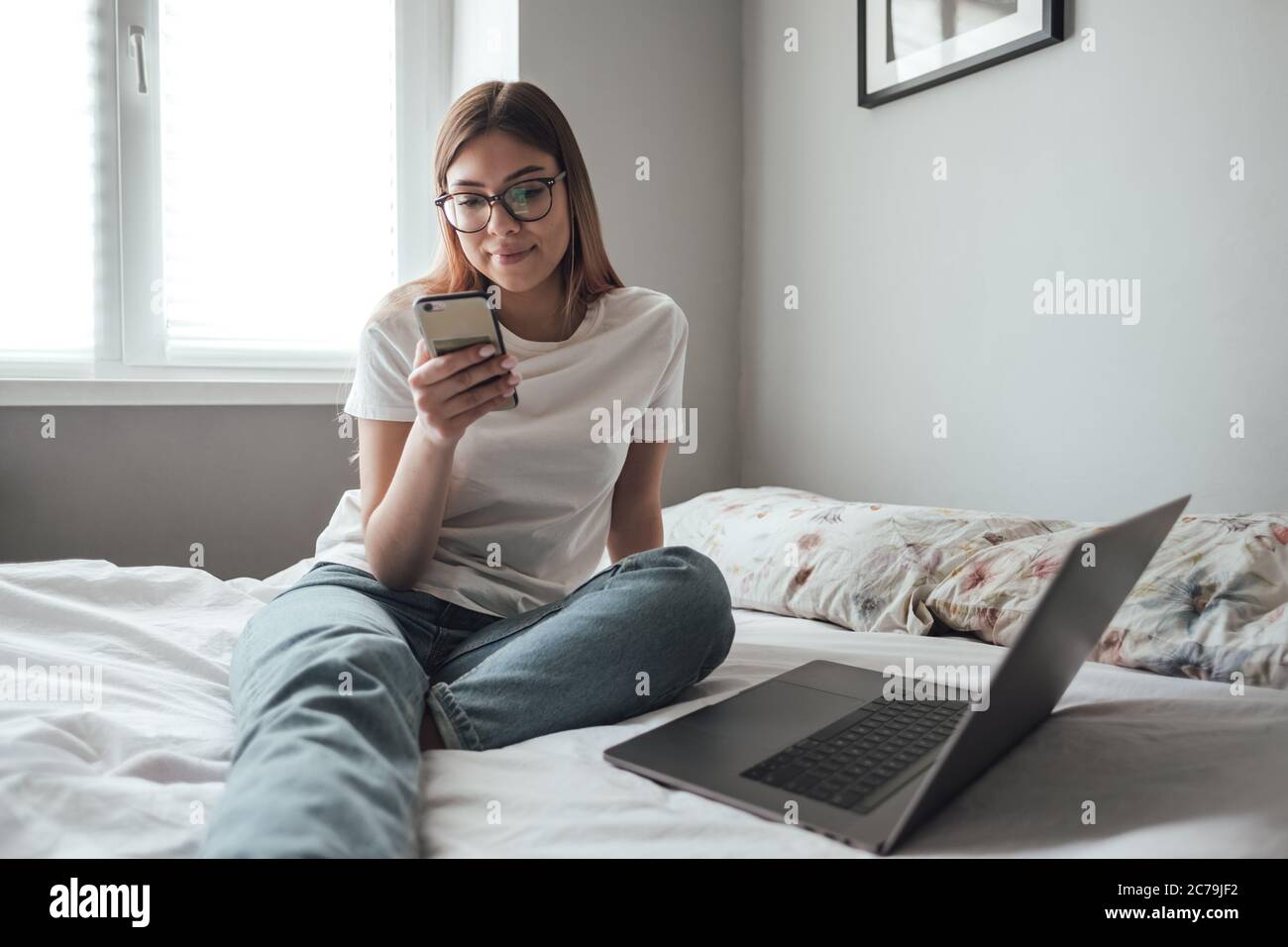 Young smiling woman use smartphone at home on the bed. Communication ...