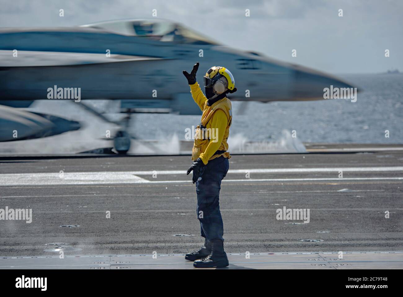 A U.S. Navy deck crew signals a F/A-18E Super Hornet fighter aircraft ...