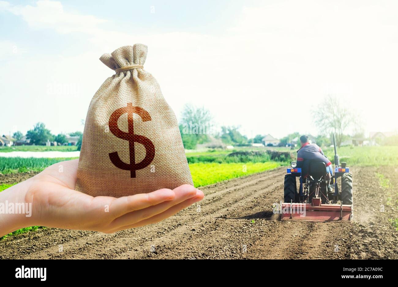 A hand holds out a dollar money bag on a background of a field ...