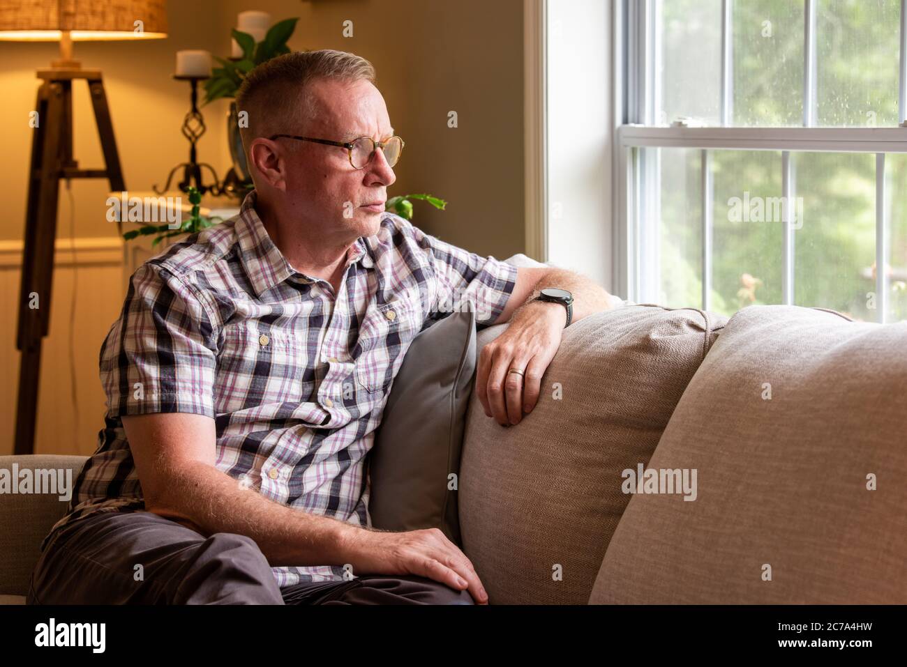 Man, seated alone in his home, looks outside. Good for concepts of ...