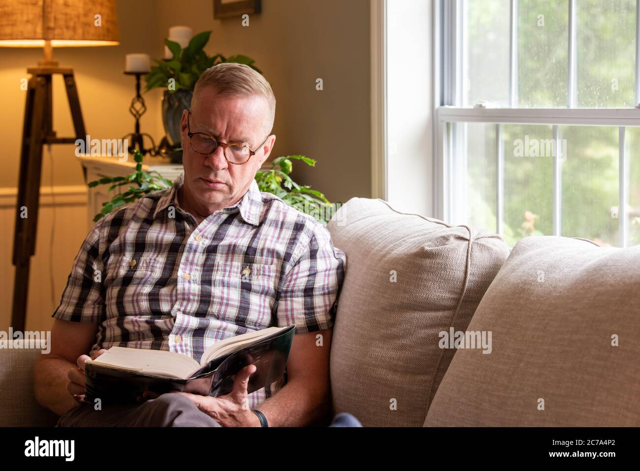 A man sits alone, inside, reading a large book Stock Photo - Alamy