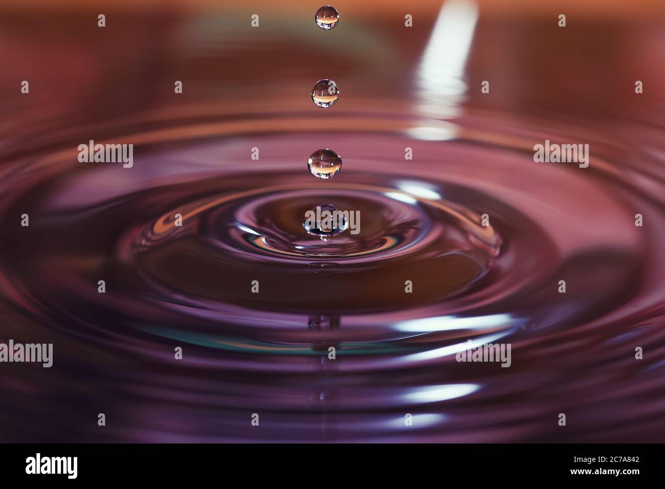 Macro photo of water drops falling into a pool of water, causing a ...