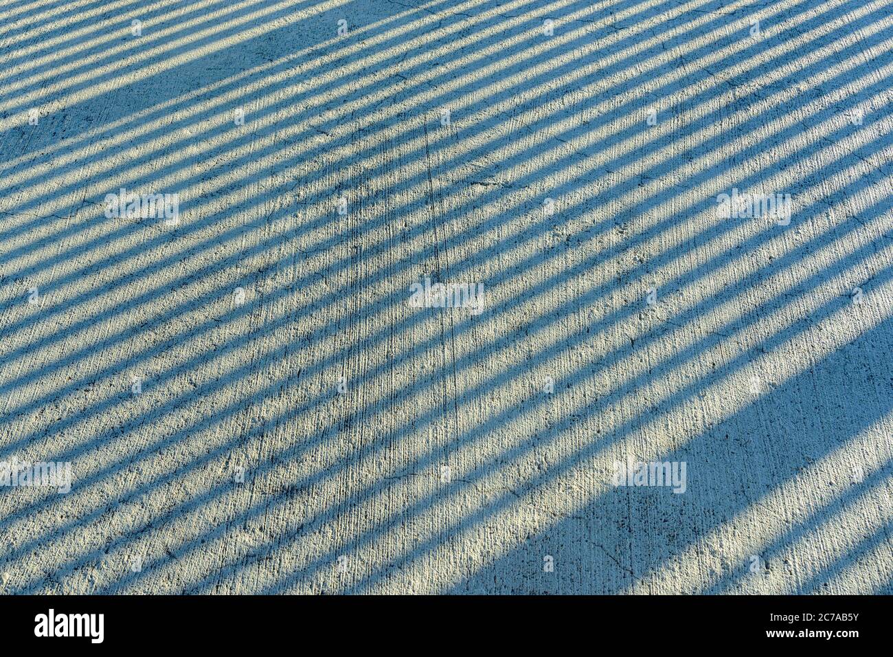 Gap step diagonal shadows from sunlight on a scratched concrete surface ...