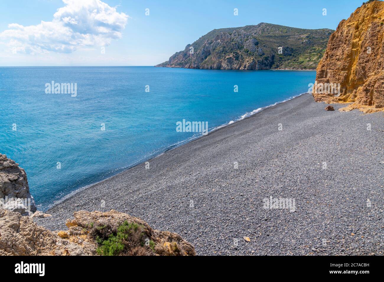An empty black beach with pebbles and blue turquoise clear, calm water ...